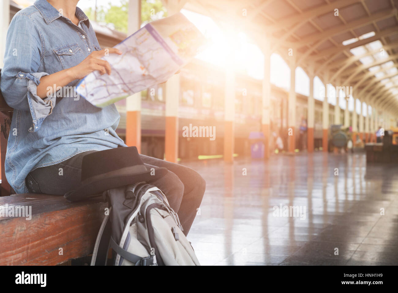 young woman holding map with backpack sitting on platform at train ...