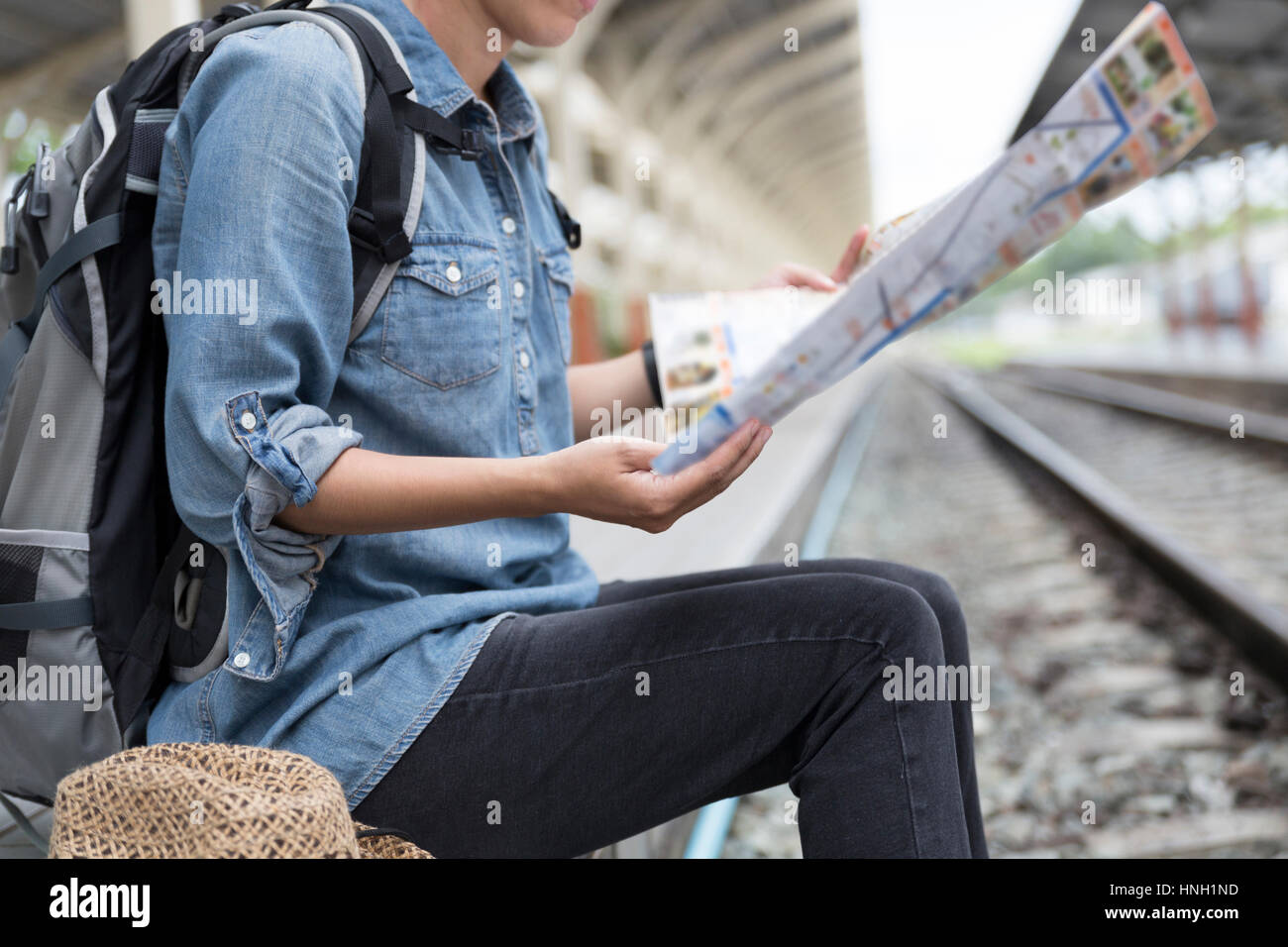 young woman holding map with backpack sitting on platform at train ...