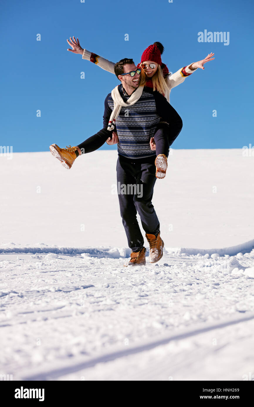Couple playing in snow. Man giving woman piggyback ride on winter ...
