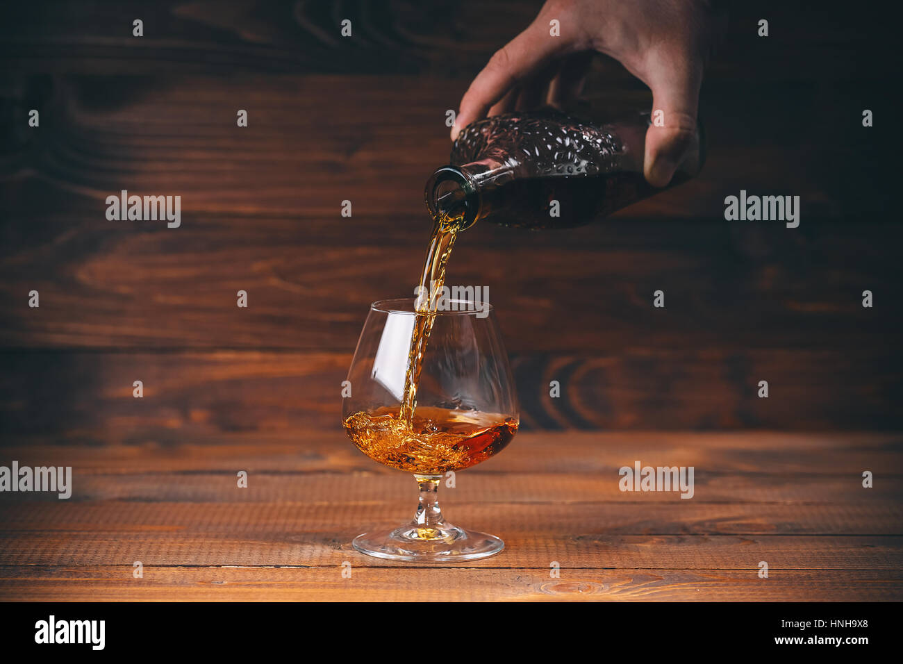Pouring brandy or cognac from the bottle into the glass against wooden ...