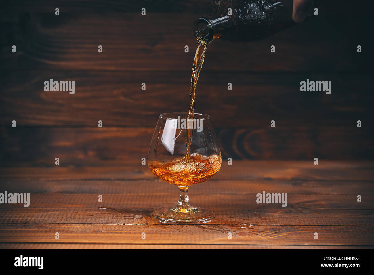 Pouring brandy or cognac from the bottle into the glass against wooden ...