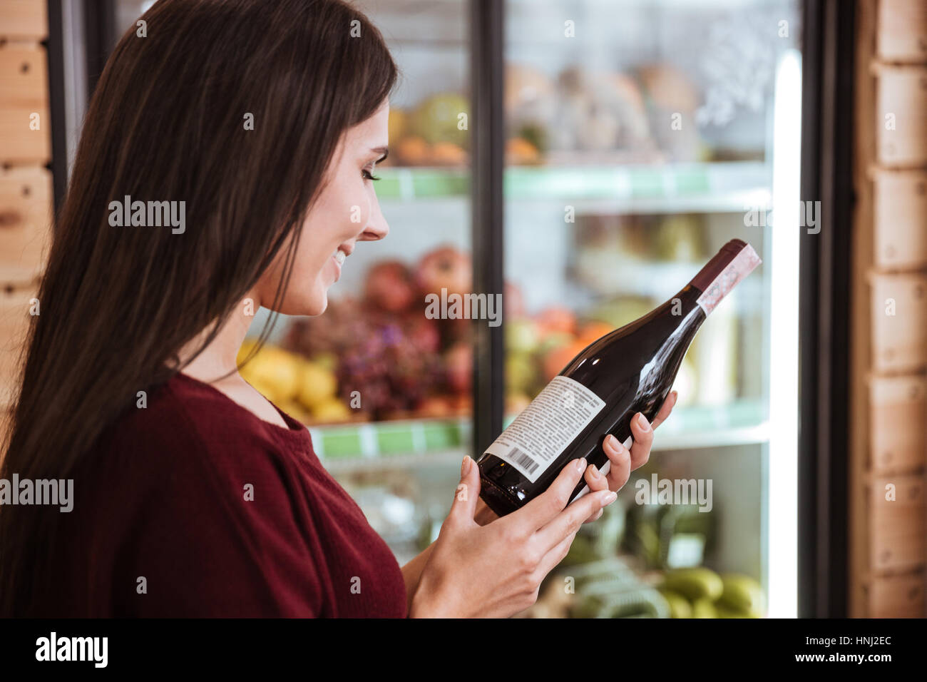 Attractive young woman standing and choosing wine in grocery shop Stock ...