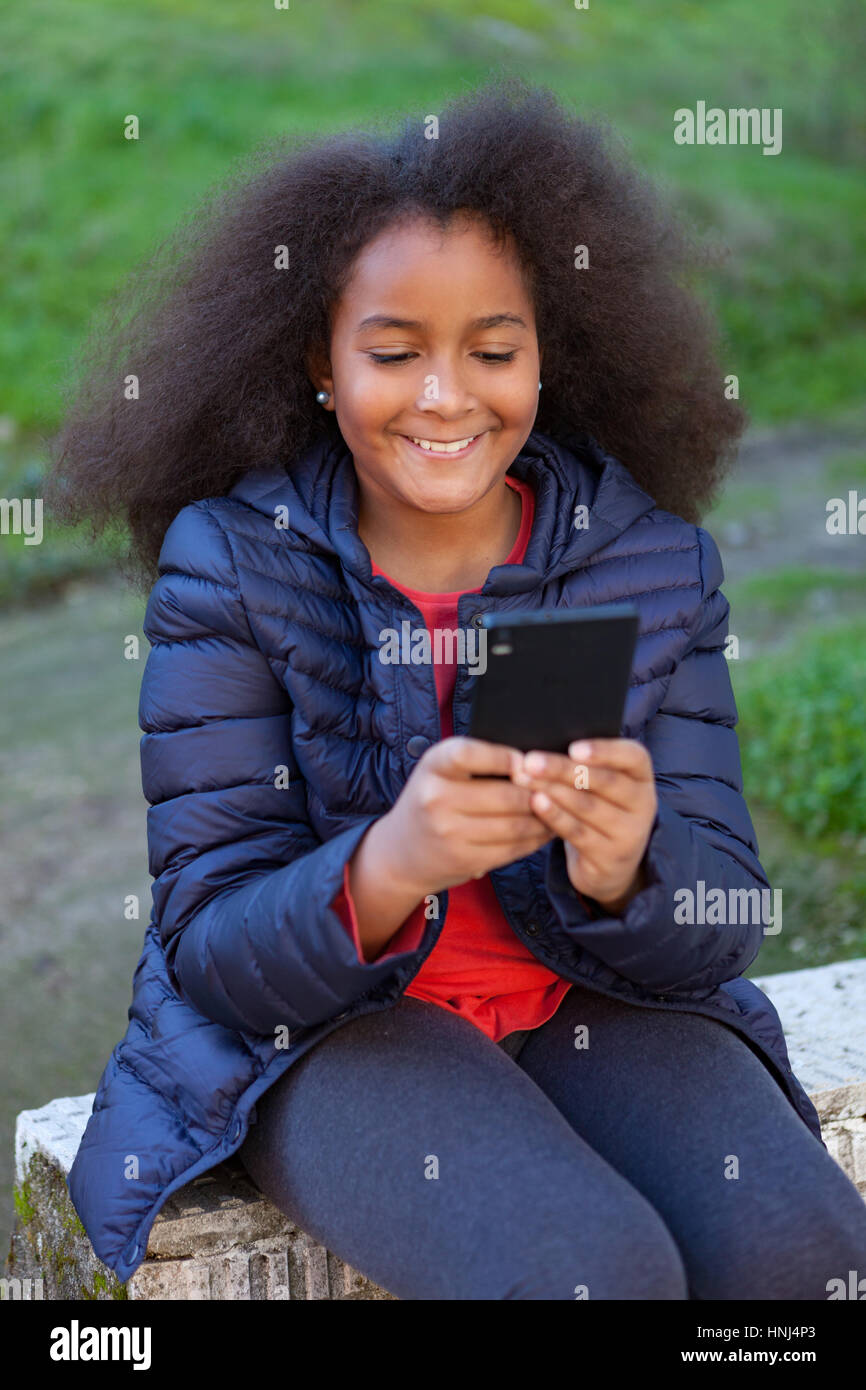 Smiling afro child with a mobile in the park taking a photo himself ...