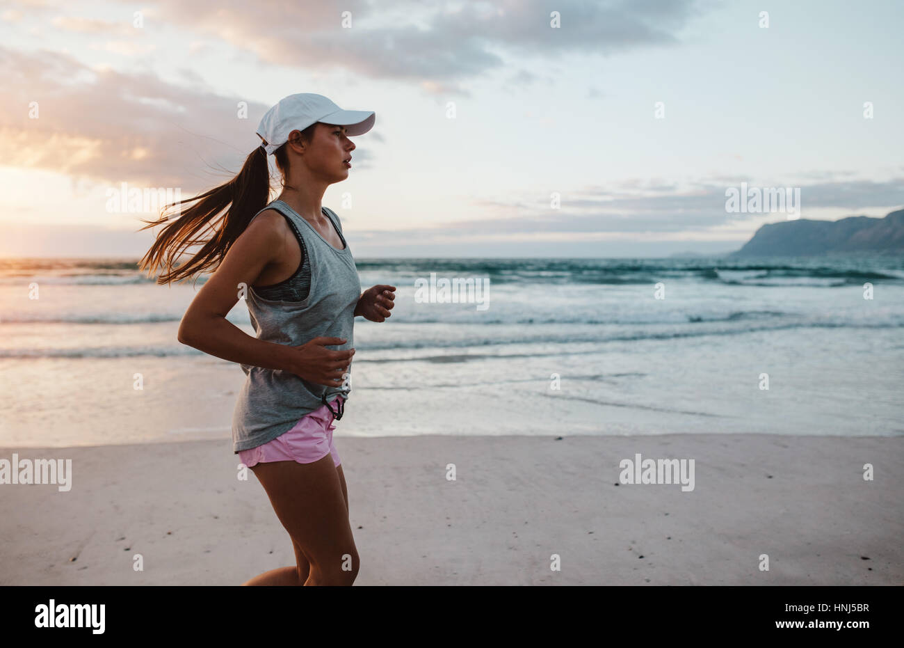 Side view shot of fit young woman jogging at the beach in the morning ...