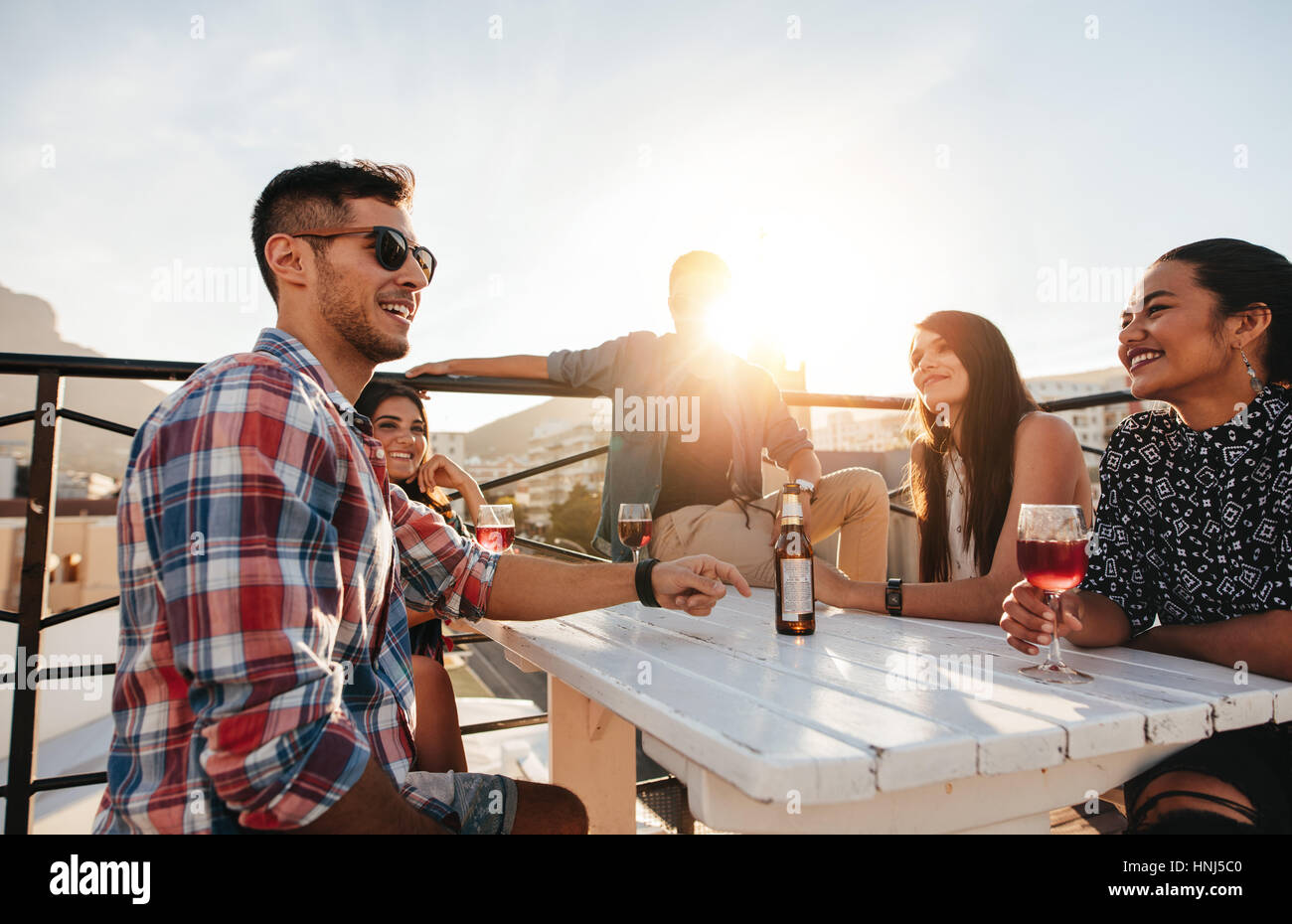 Group of friends sitting around a table at rooftop party. Young people ...