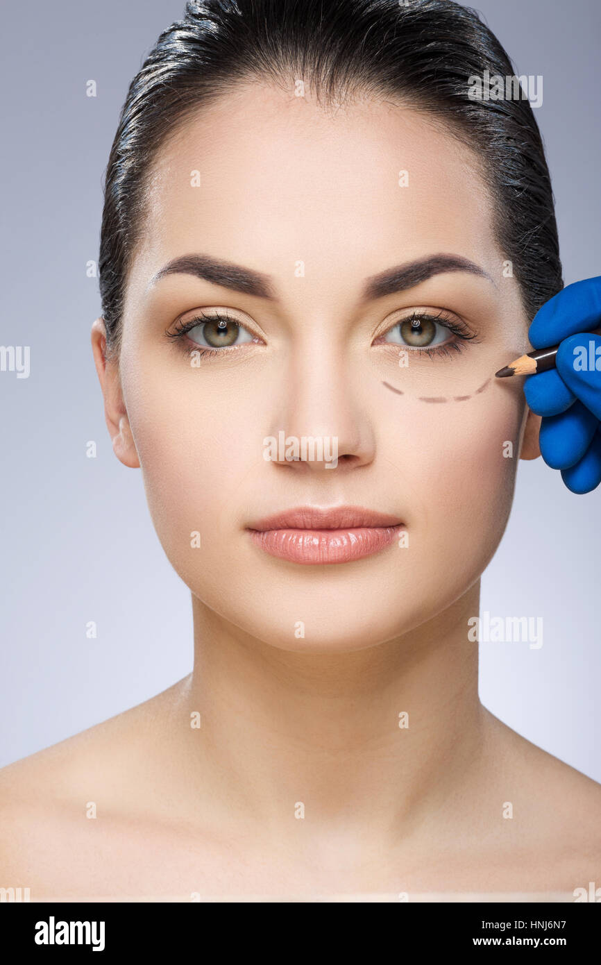 Plastic surgeon drawing line under eye Stock Photo - Alamy