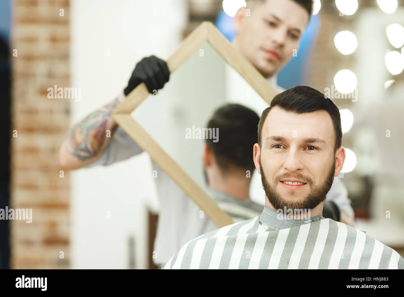 Barber holding a mirror for client Stock Photo - Alamy