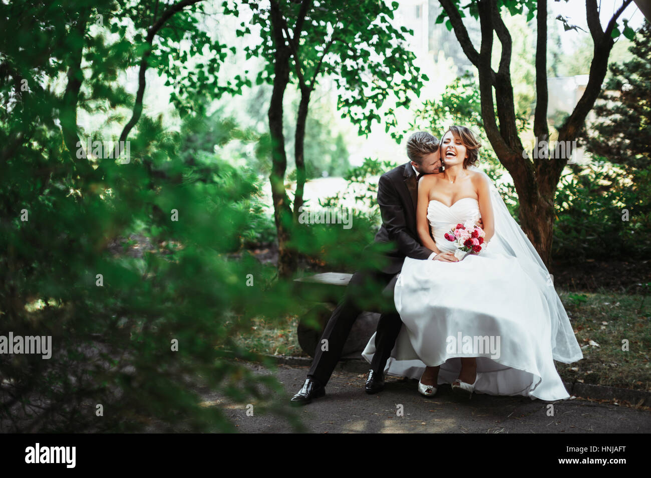 Bride and groom sitting on bench in park Stock Photo - Alamy