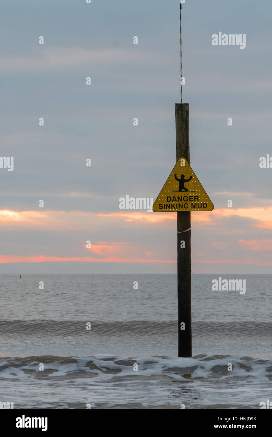 Danger Sinking Mud sign in front of waves and sunset. Warning of ...