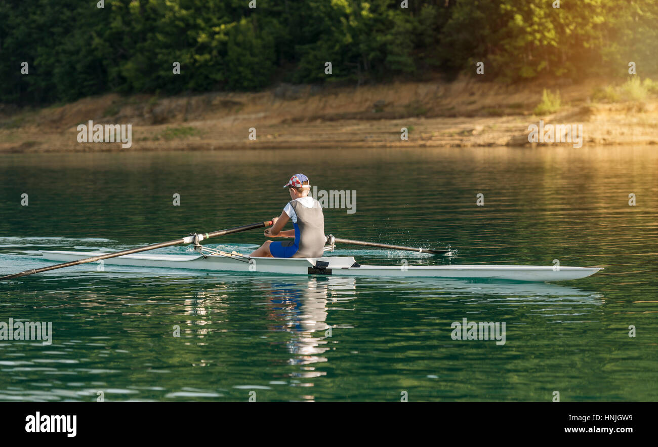 A Young single scull rowing competitor paddles on the tranquil lake ...