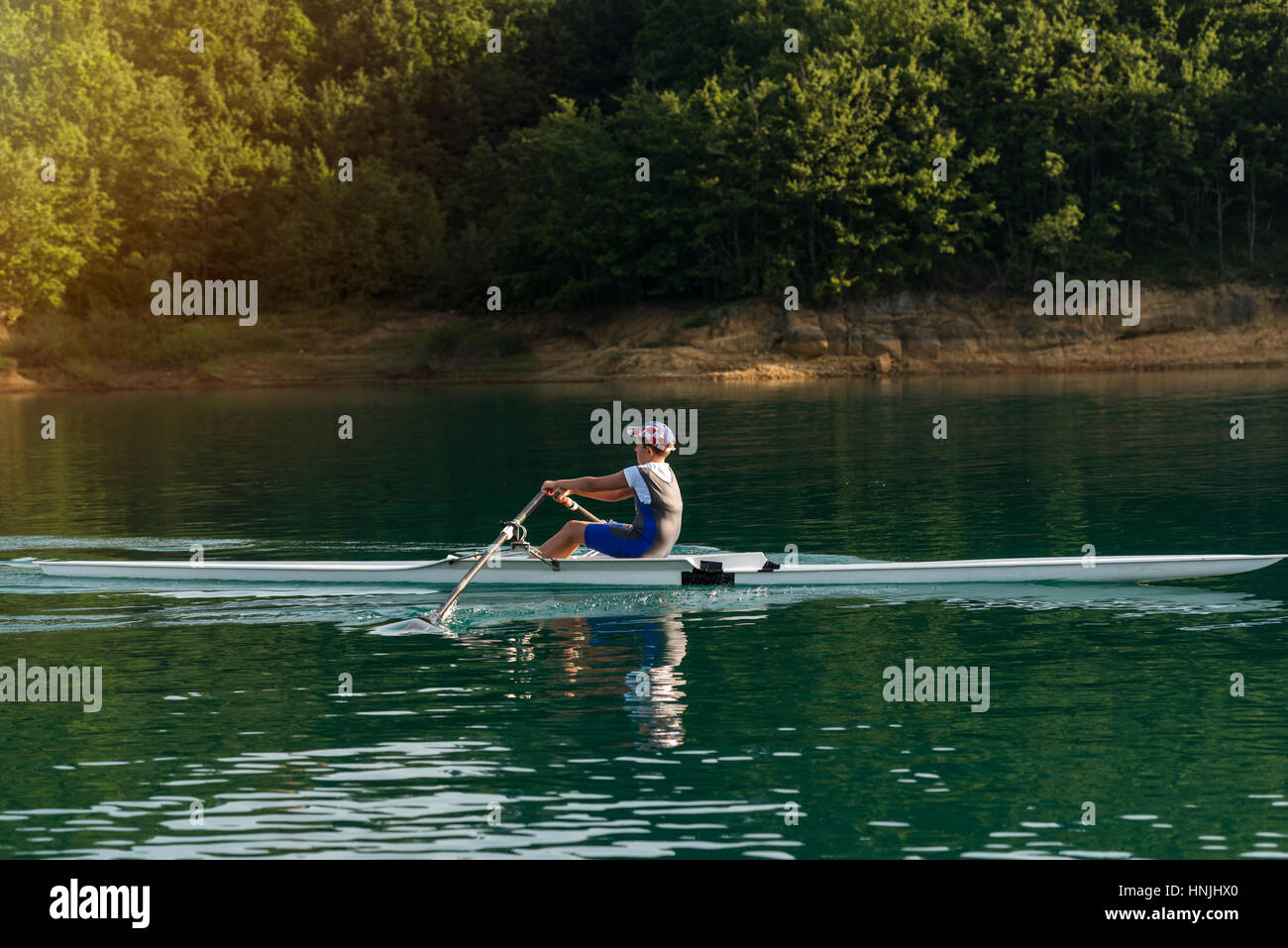 A Young single scull rowing competitor paddles on the tranquil lake ...