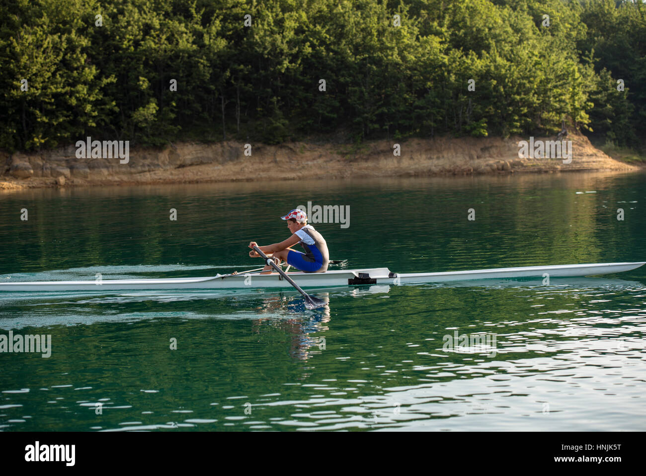 A Young single scull rowing competitor paddles on the tranquil lake ...