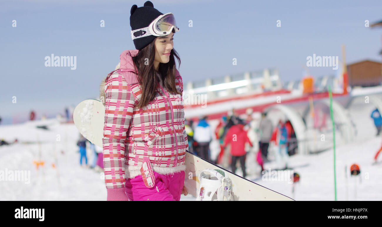 Cute and happy female asian snowboarder walking with her board on snowy ...