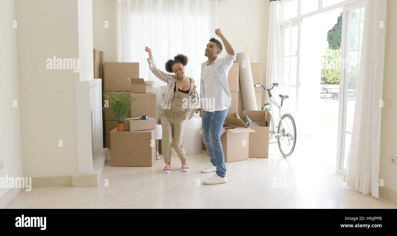 Young couple dancing for joy in the living room of their new home with ...