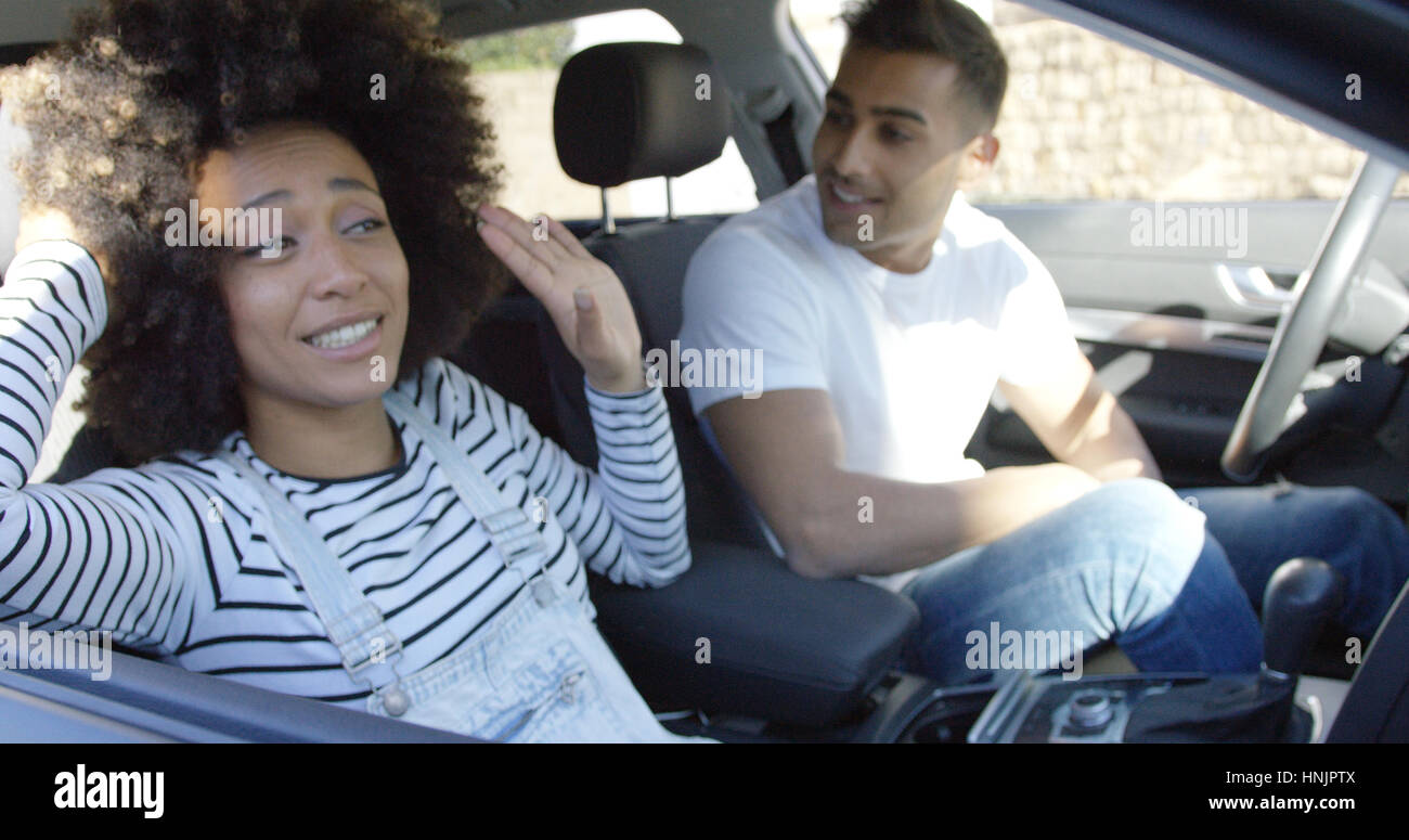 Playful young woman goofing around in a car watched by her smiling ...