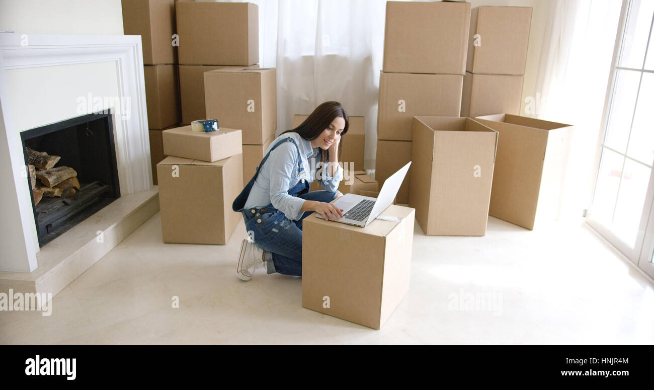 Young woman using a laptop on a cardboard box as she catches up with ...