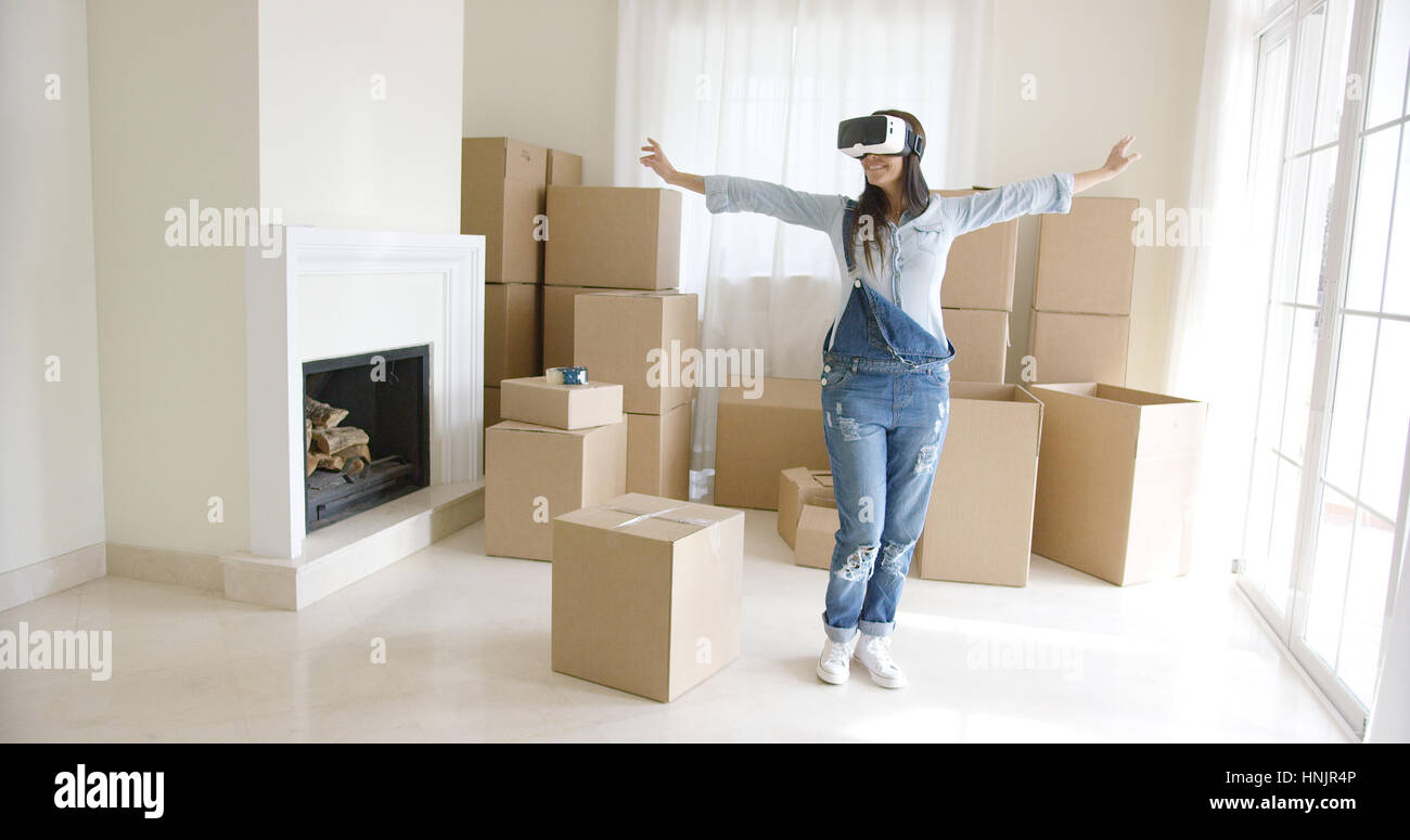 Happy young woman enjoying her VR headset prancing around in a room ...