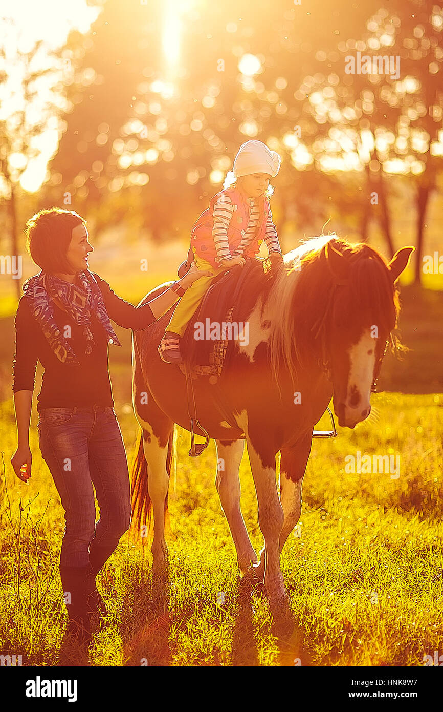 Little girl riding on a horseback with her mother walking nearby Stock ...