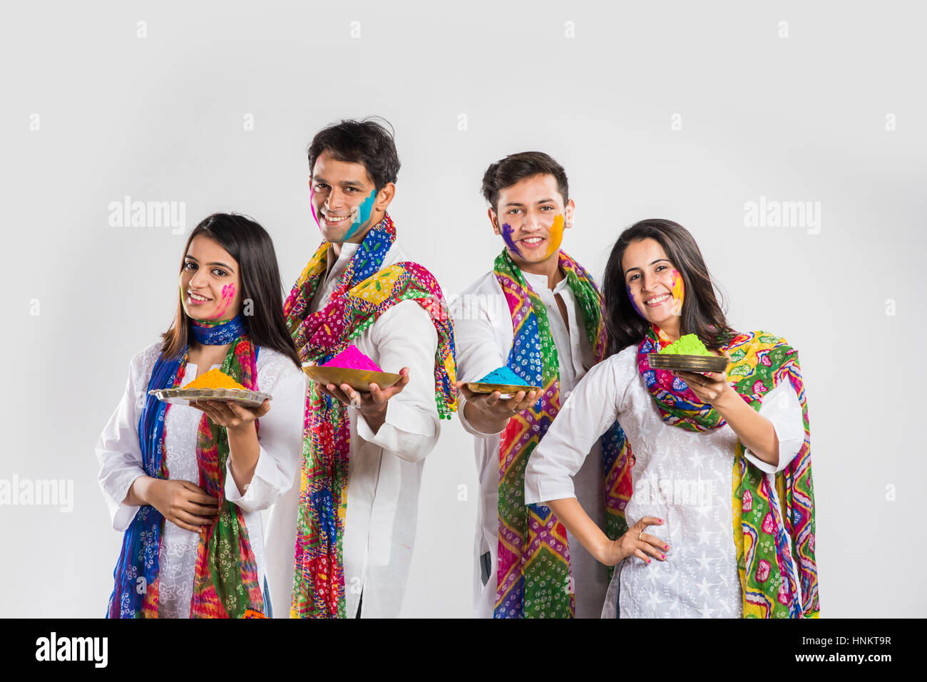 4 smart young indian people celebrating holi, standing isolated over ...