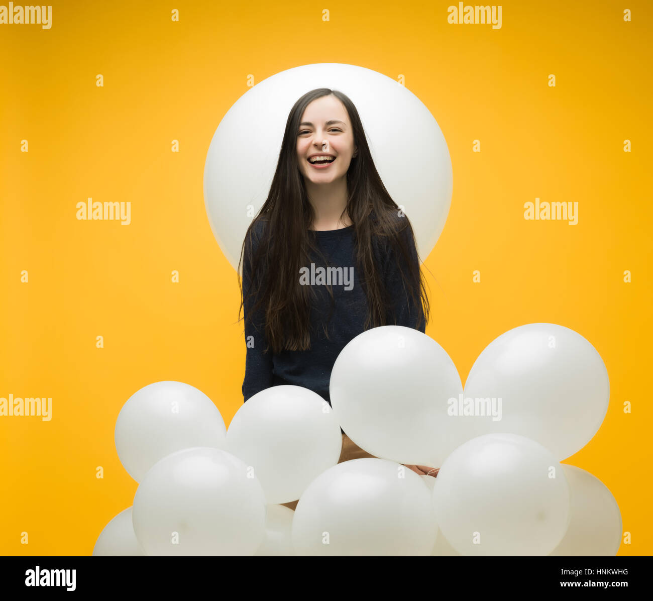 young brunette with long hair laughing with white balloons in her hands ...