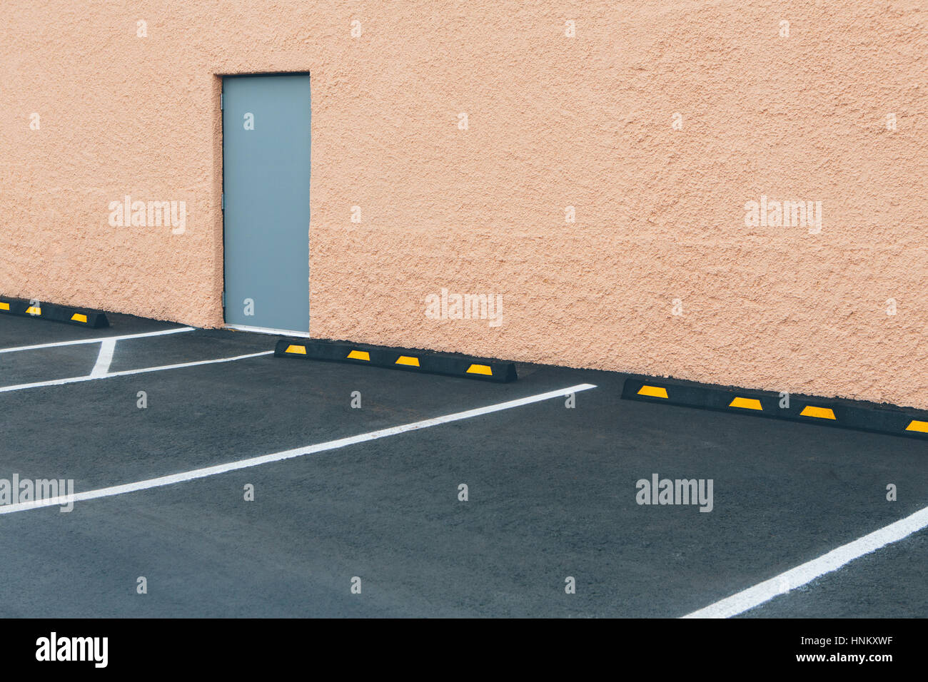 A car park with lined bays outside a building, and a door in a wall ...