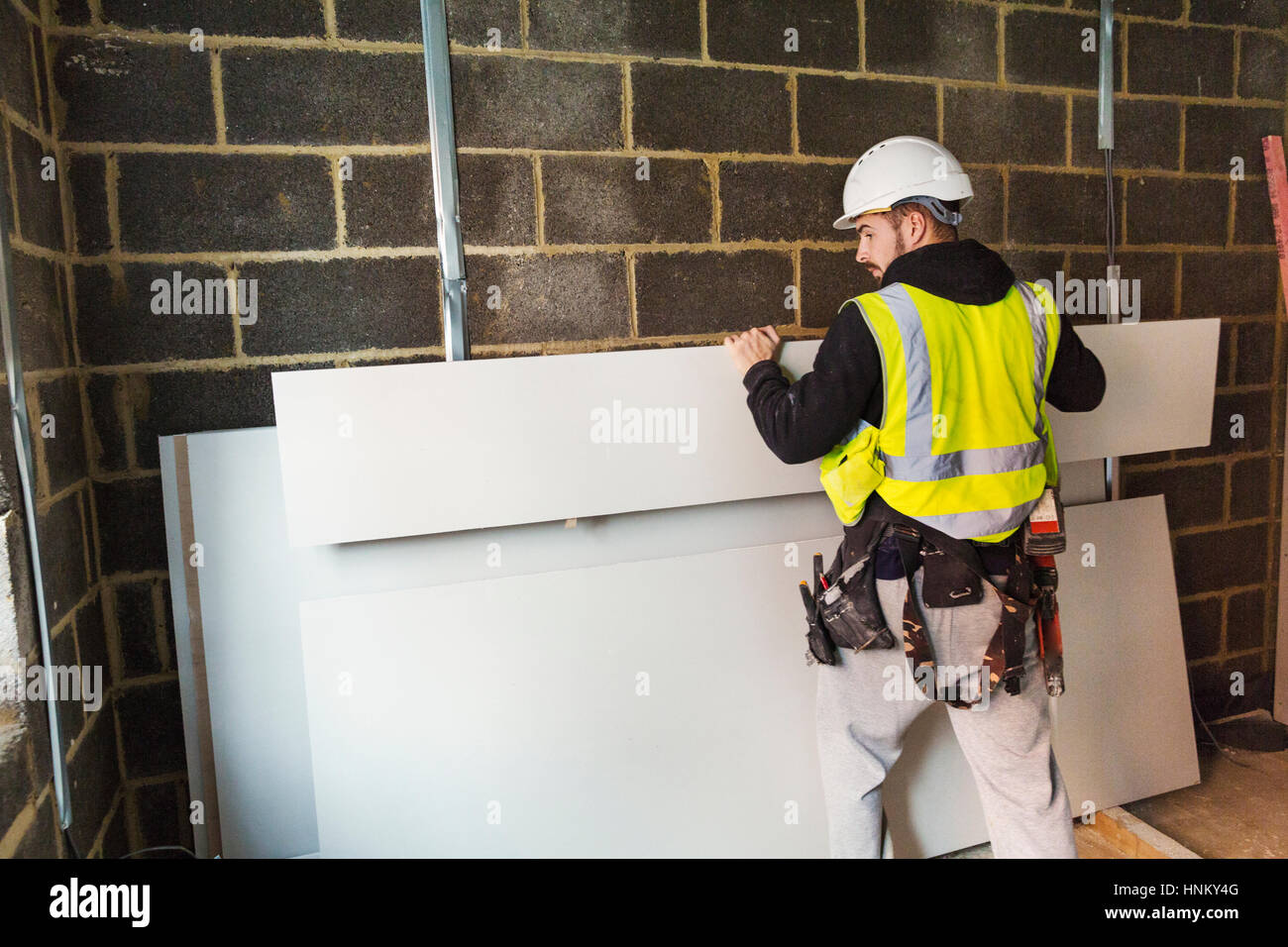 A workman in hard hat and high vis jacket stacking wood against a wall ...