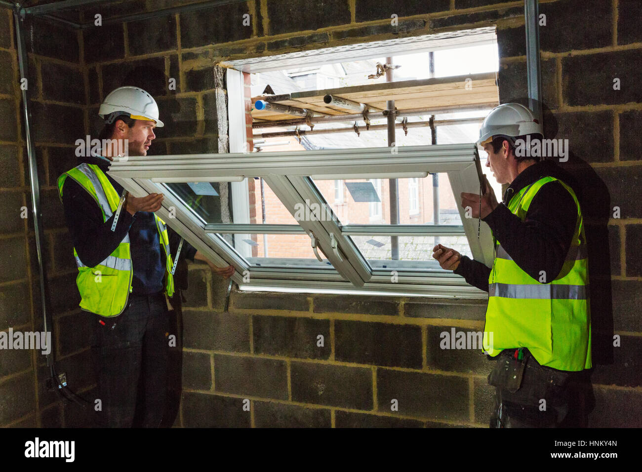 Two builders in hard hats and high visibility jacket fitting a window ...