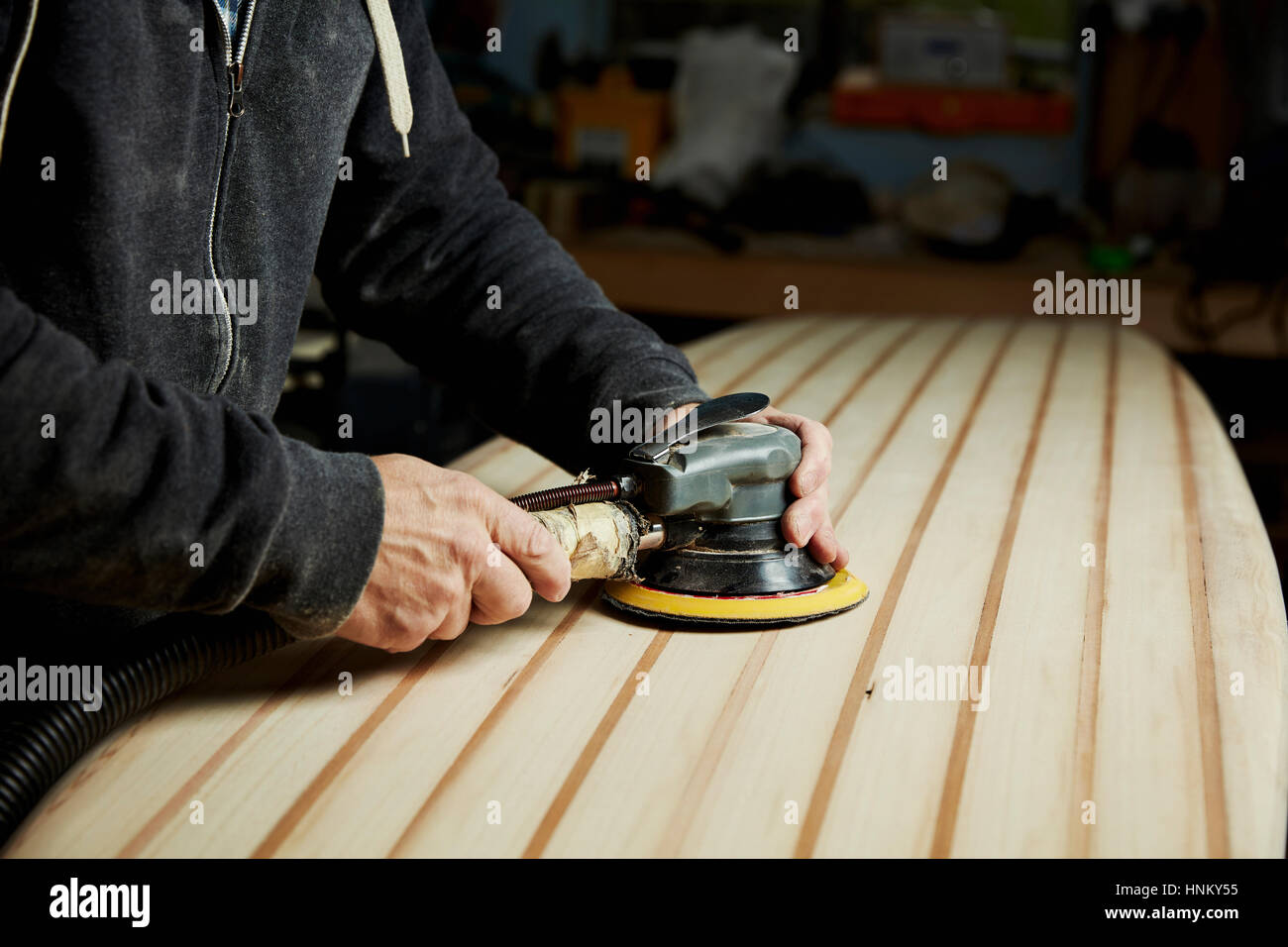 A man finishing the surface of a wooden surfboard with an electrical ...