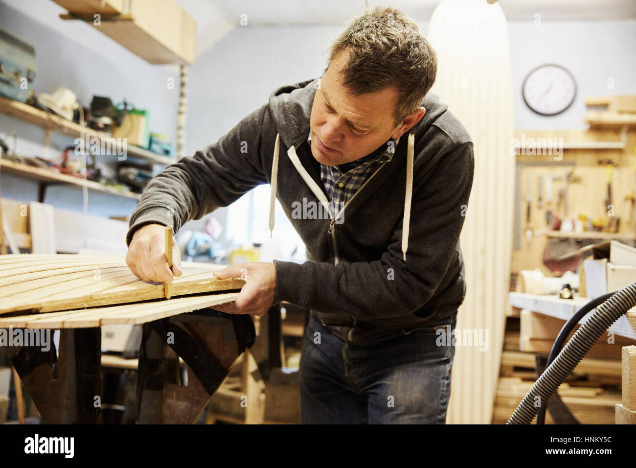 Man working on the edge of a wooden shaped board in a woodwork shop ...