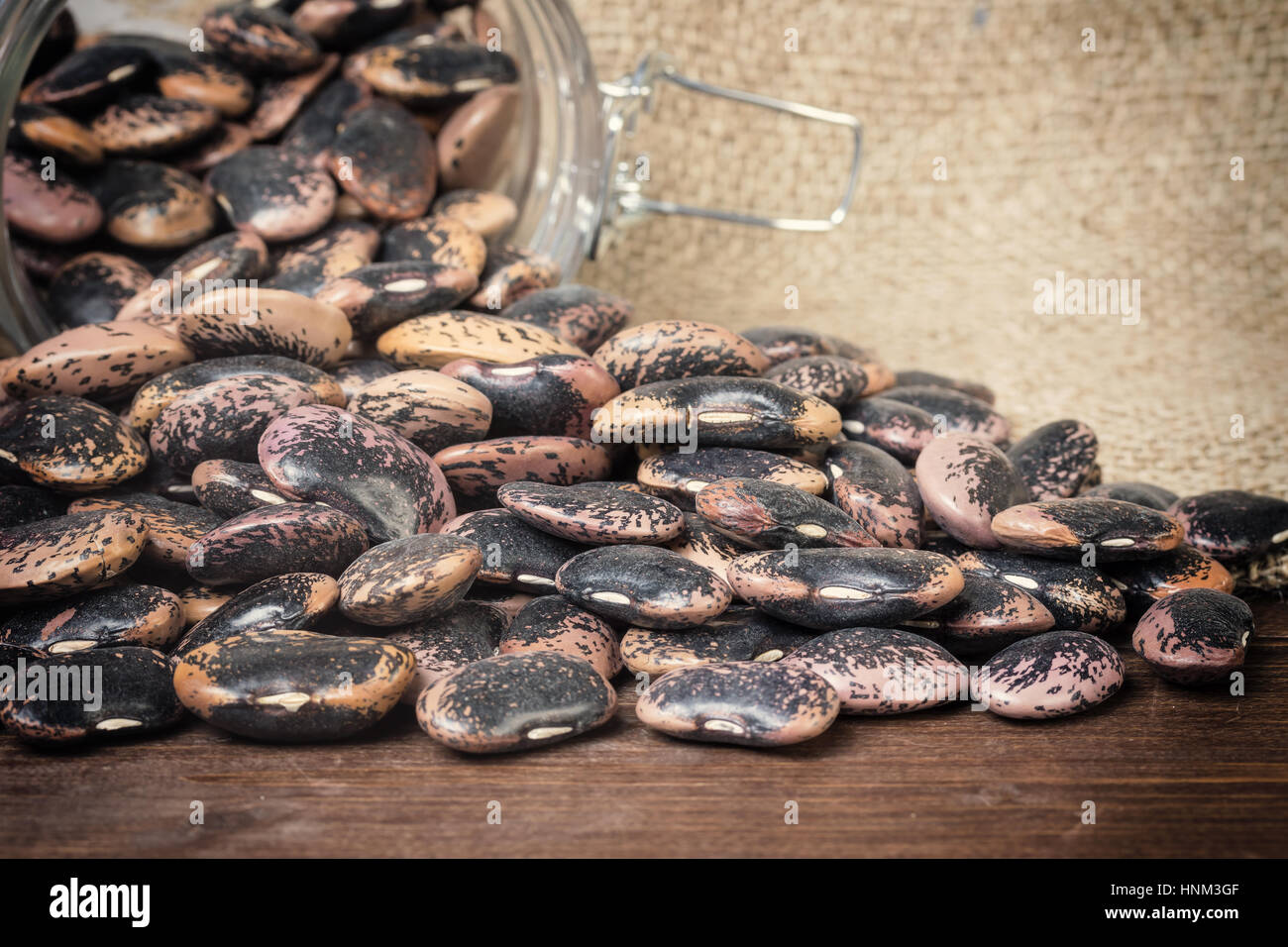 Beans spilled from the lying glass on burlap sack and wooden desk ...