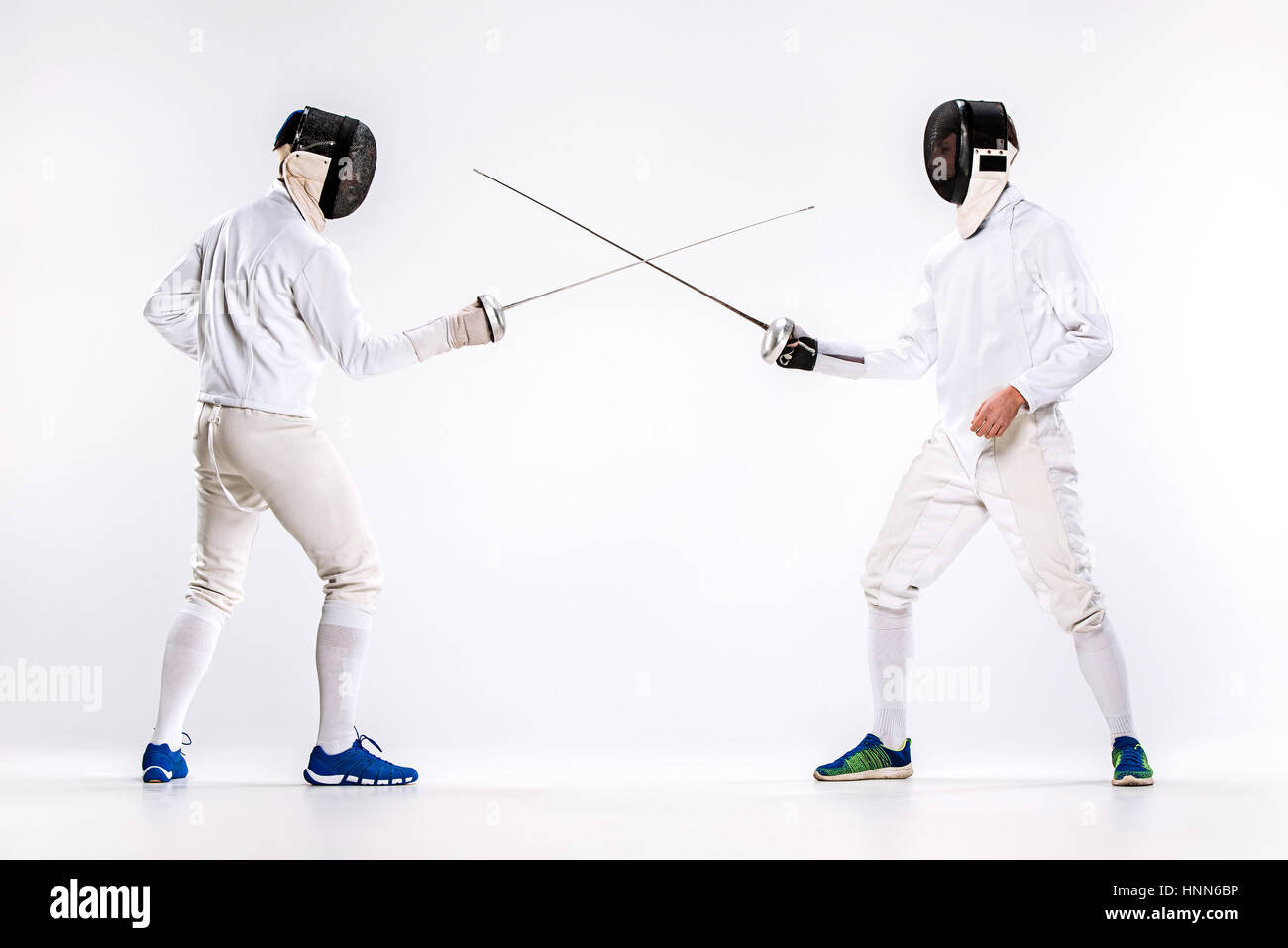 The two men wearing fencing suit practicing with sword against gray ...