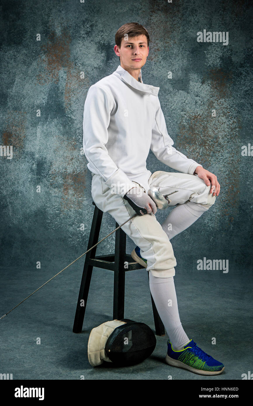 The man wearing fencing suit posing with sword against gray studio ...