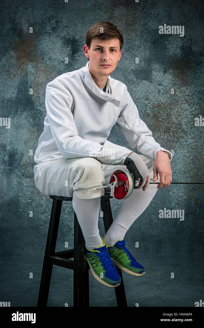 The man wearing fencing suit posing with sword against gray studio ...