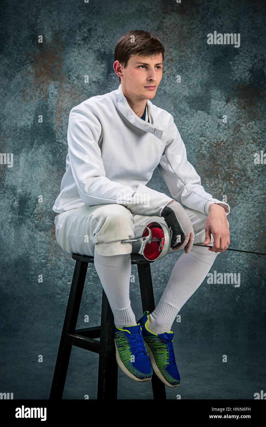 The man wearing fencing suit posing with sword against gray studio ...