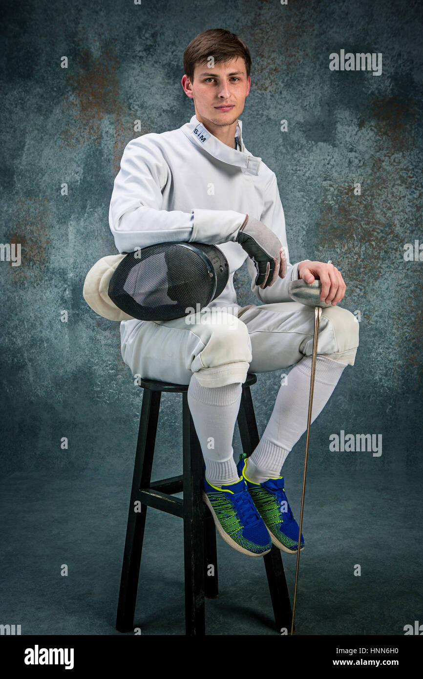 The man wearing fencing suit posing with sword against gray studio ...