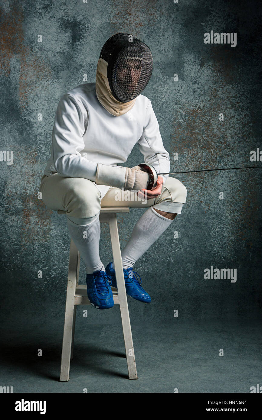 The man wearing fencing suit posing with sword against gray studio ...