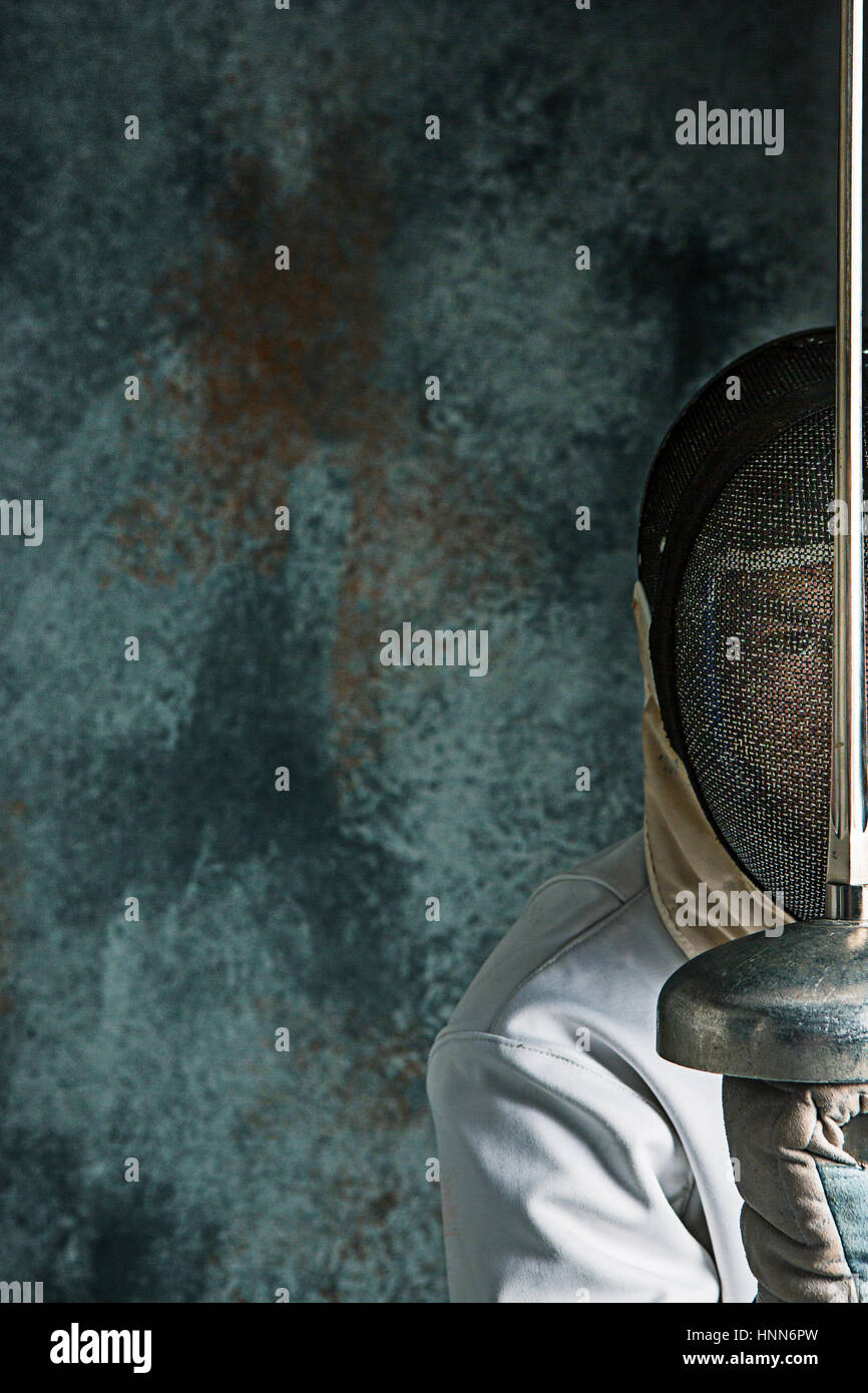 The man wearing fencing suit posing with sword against gray studio ...
