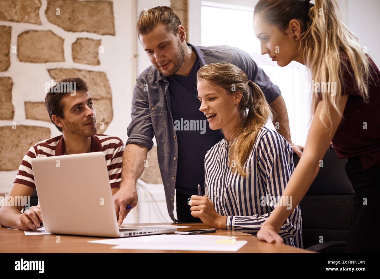 Young business team sitting and standing around a laptop computer while ...