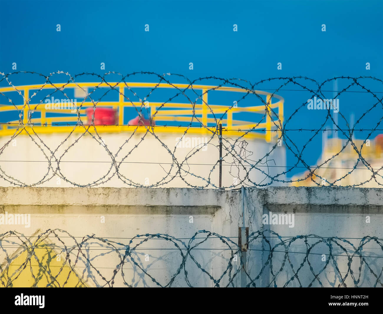 The barbed wire on the fence near the oil tanks Stock Photo - Alamy