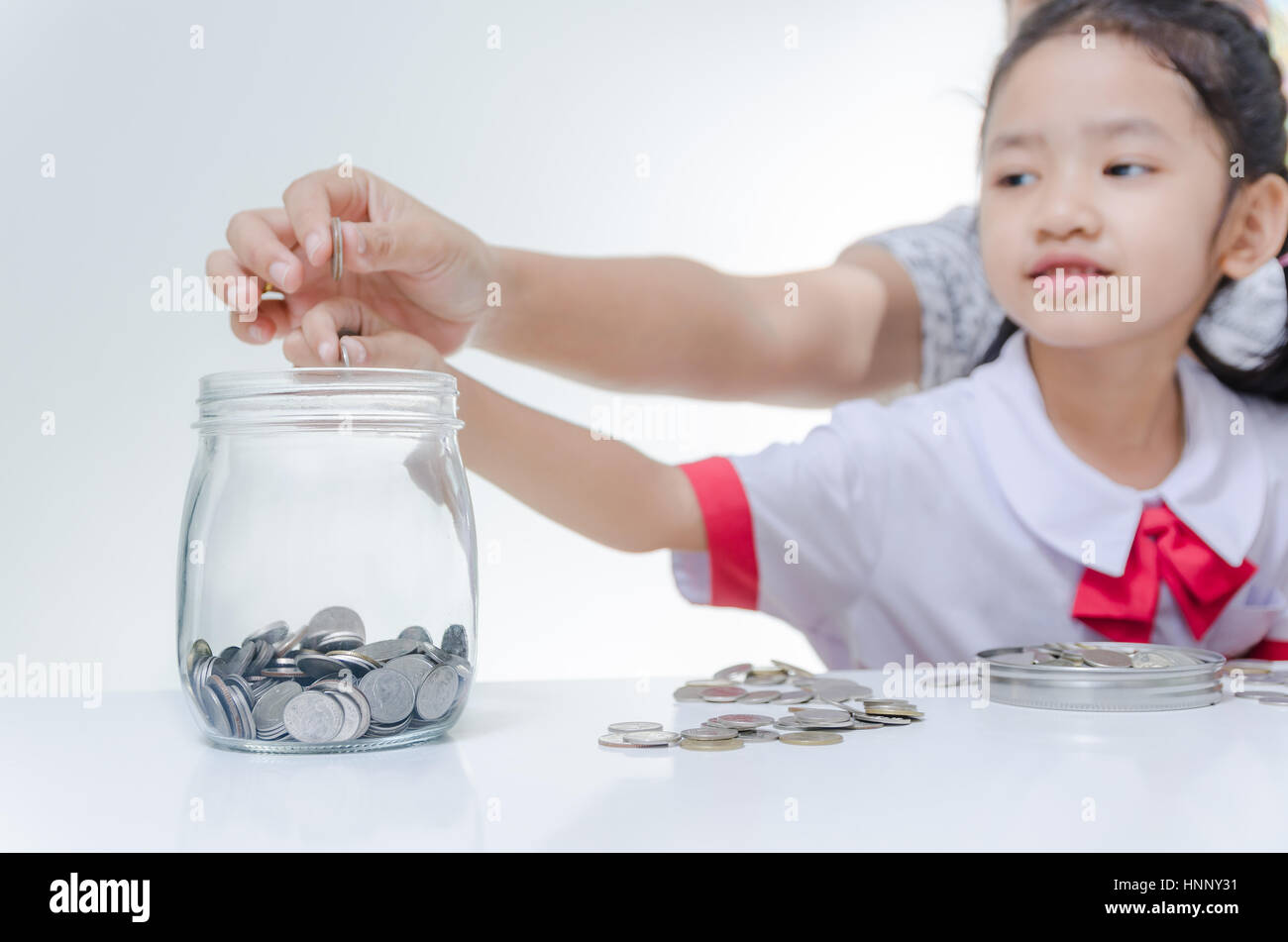 Asian little girl in Thai student uniform putting coin to glass jar ...