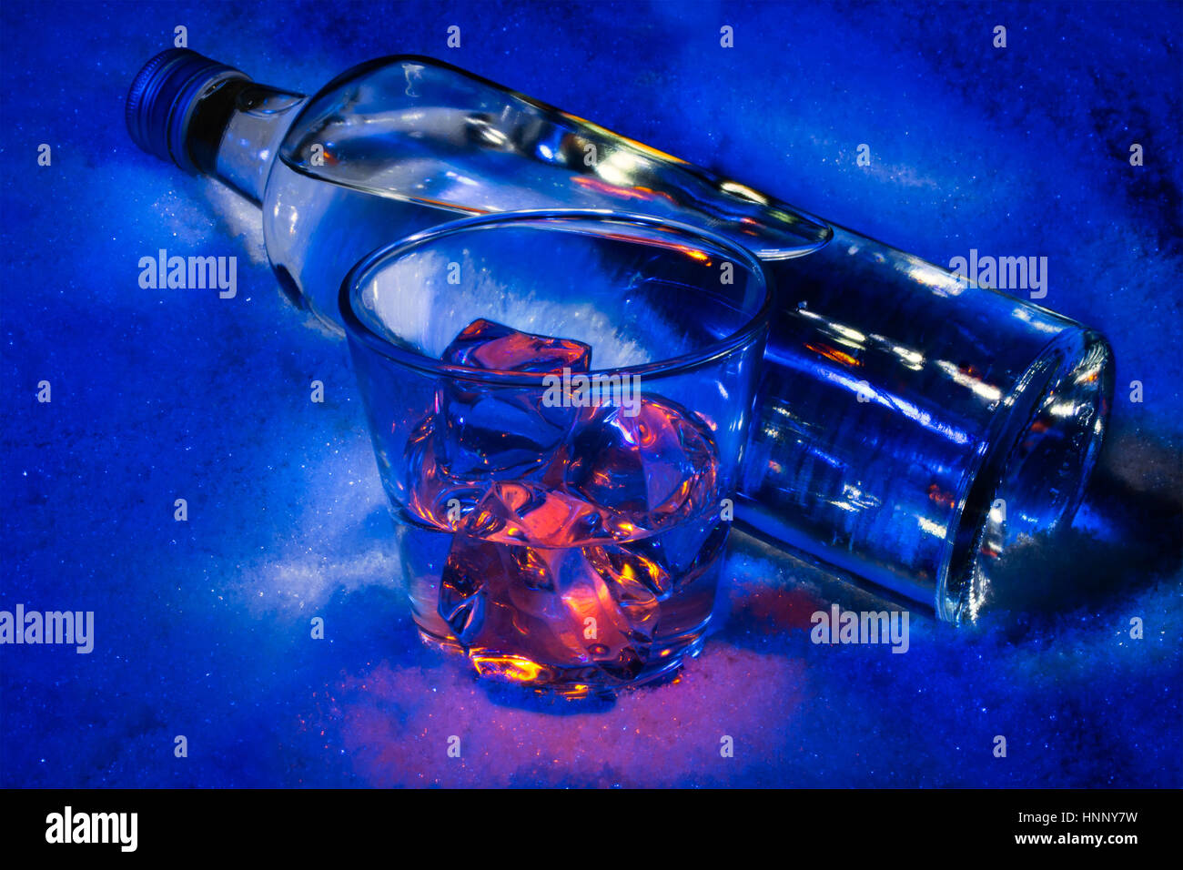 Bottle of vodka in the snow with glass filled with ice cubes, dark blue ...