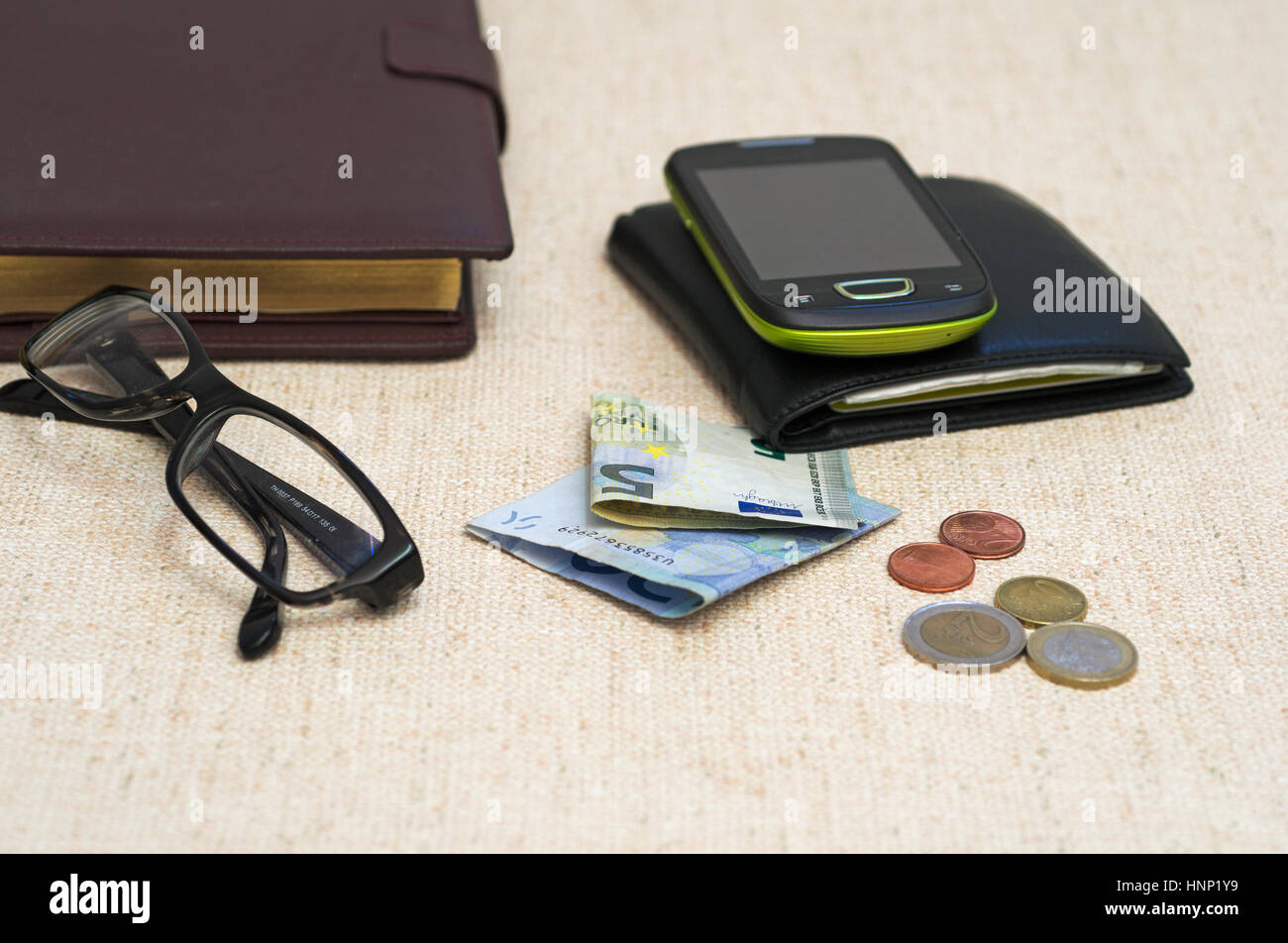 Wallet, money, mobile phone, day planner and reading glasses on table ...