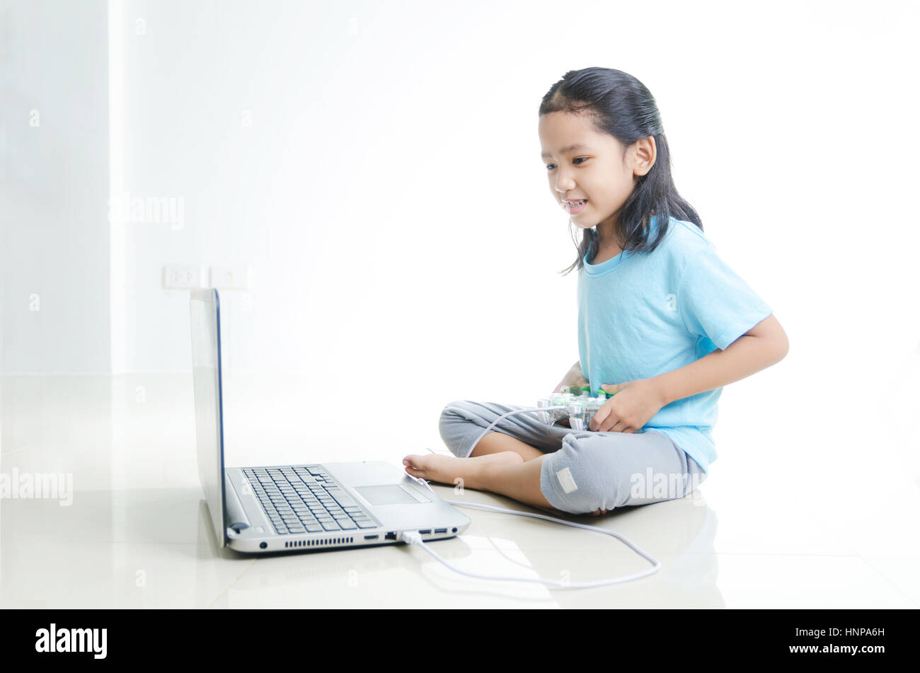 Asian little girl playing games with laptop computer and joystick ...