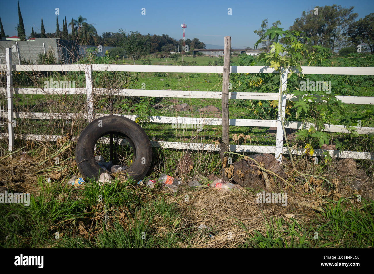 A white fence in the middle empty lot with trash piling up over it ...