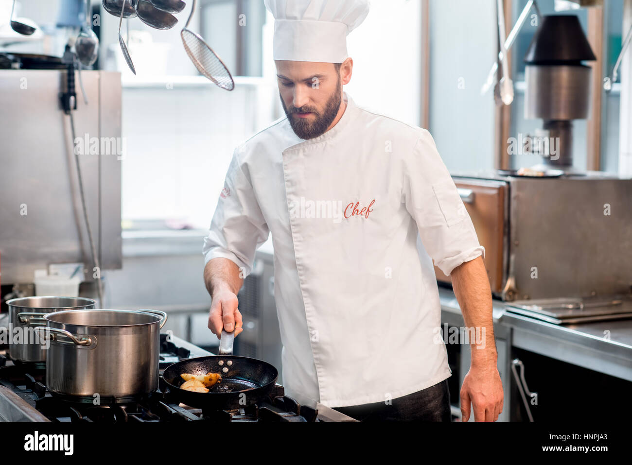 Handsome chef cook in uniform cooking food on the gas stove at the ...