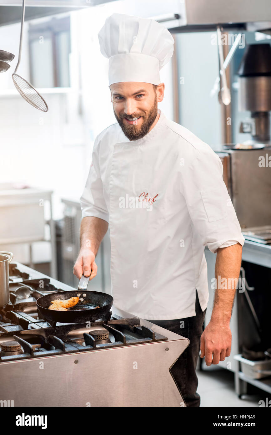 Handsome chef cook in uniform cooking food on the gas stove at the ...