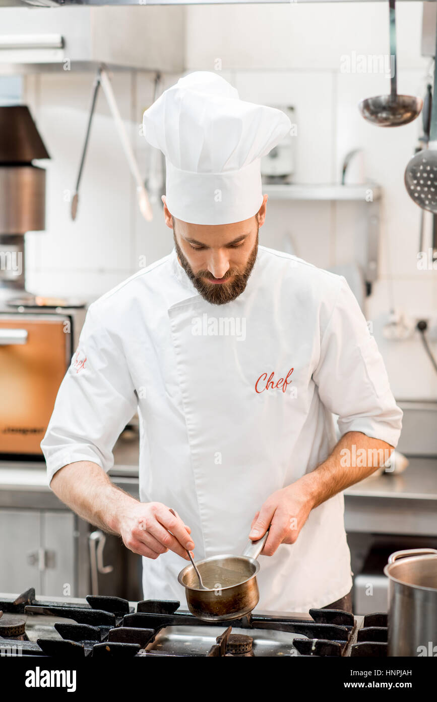 Handsome chef cook in uniform cooking food on the gas stove at the ...