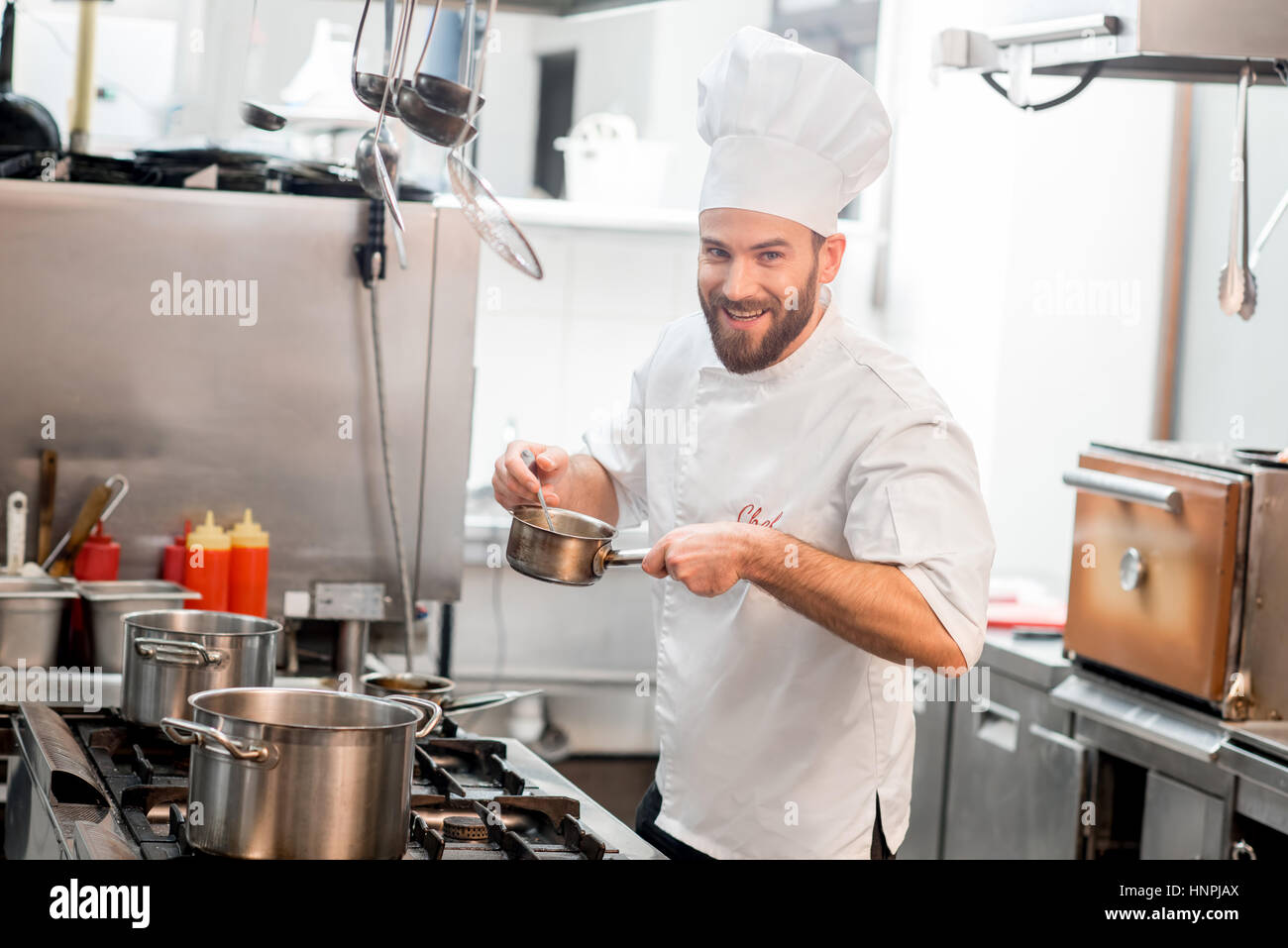 Chef cook in uniform cooking soup in the big cooker at the restaurant ...