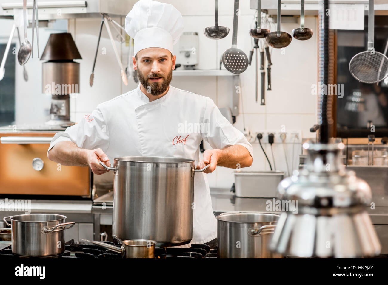 Chef cook in uniform cooking soup in the big cooker at the restaurant ...