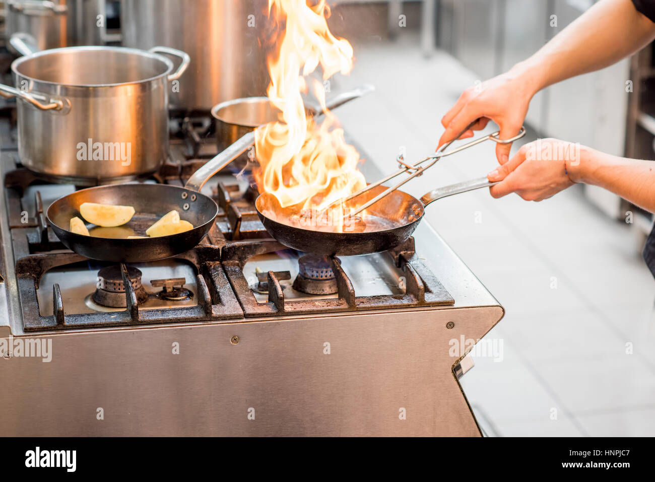 Chef frying meat steak on the gas stove with fire at the kitchen. Close ...
